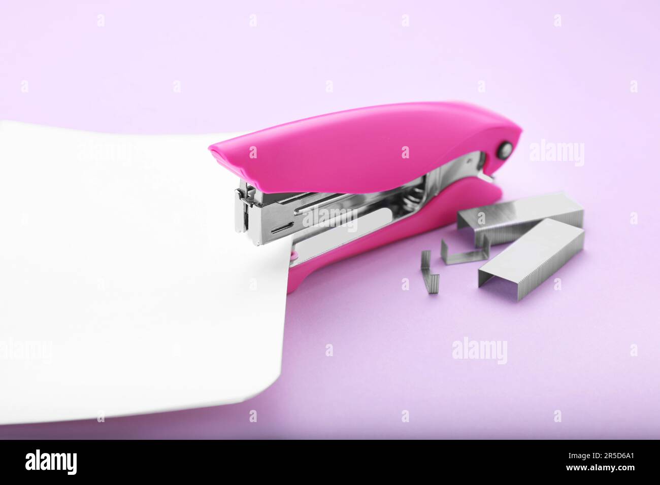 New bright stapler with paper sheet and staples on violet background ...