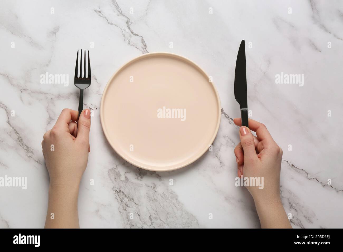 Woman with empty plate and cutlery at white marble table, top view ...