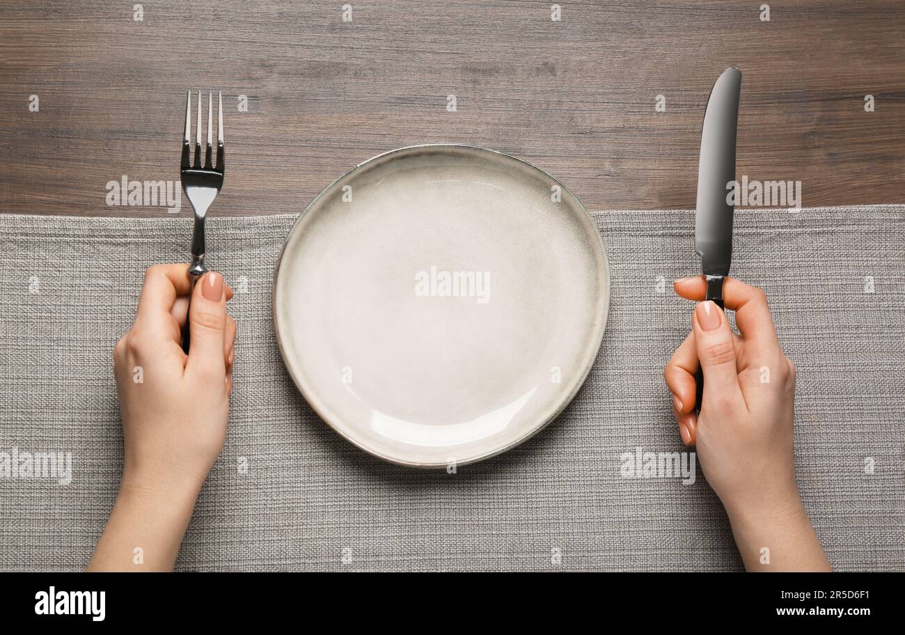 Woman with empty plate and cutlery at wooden table, top view Stock ...