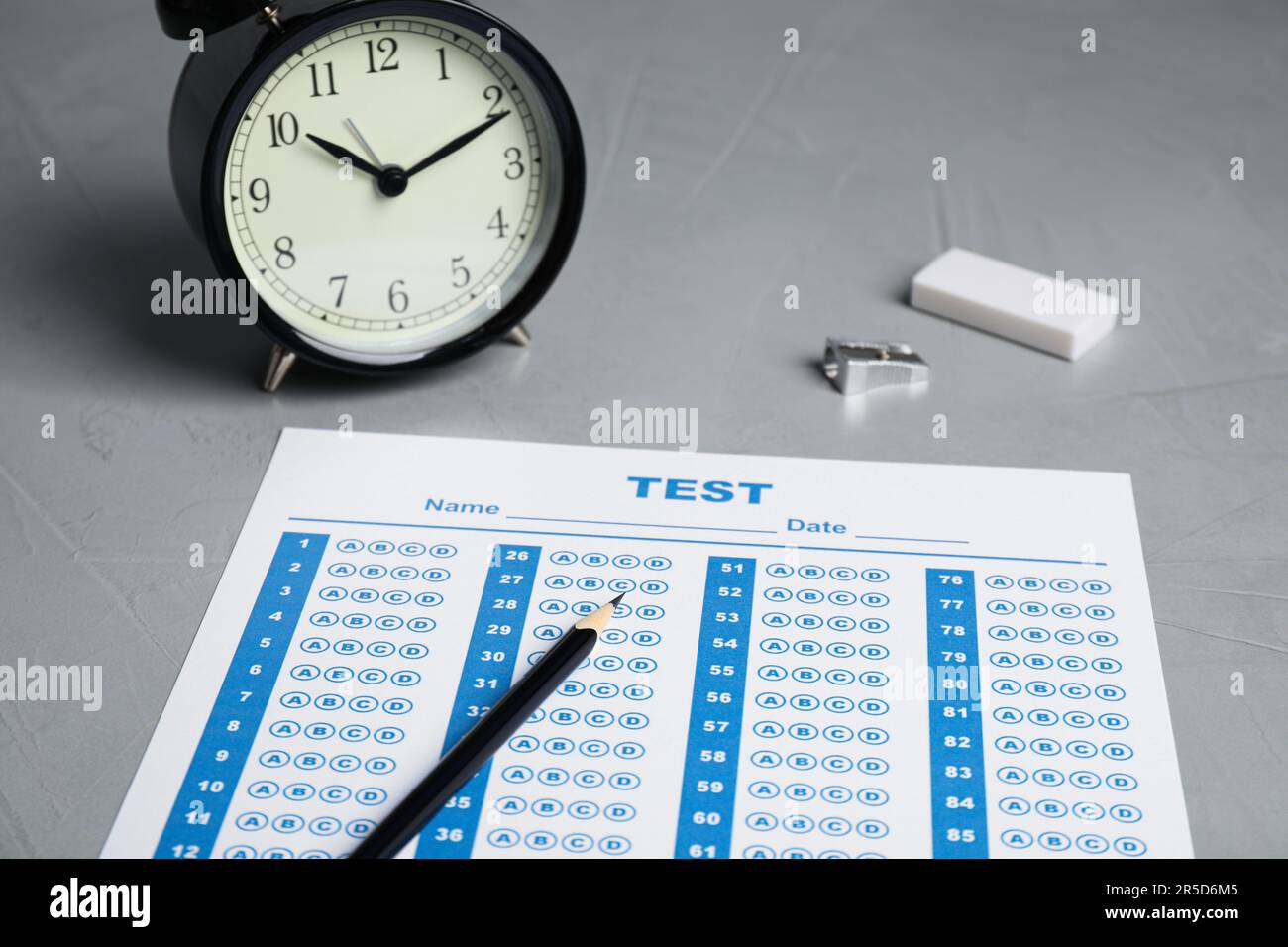Answer sheet, pencil and alarm clock on light grey table. Student ...