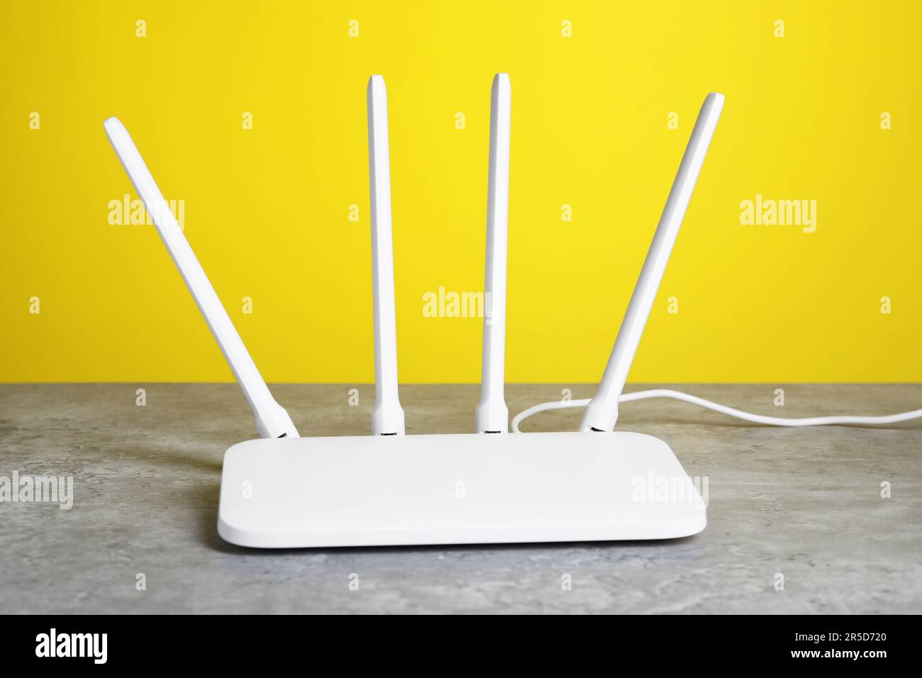 New white Wi-Fi router on grey textured table against yellow background ...
