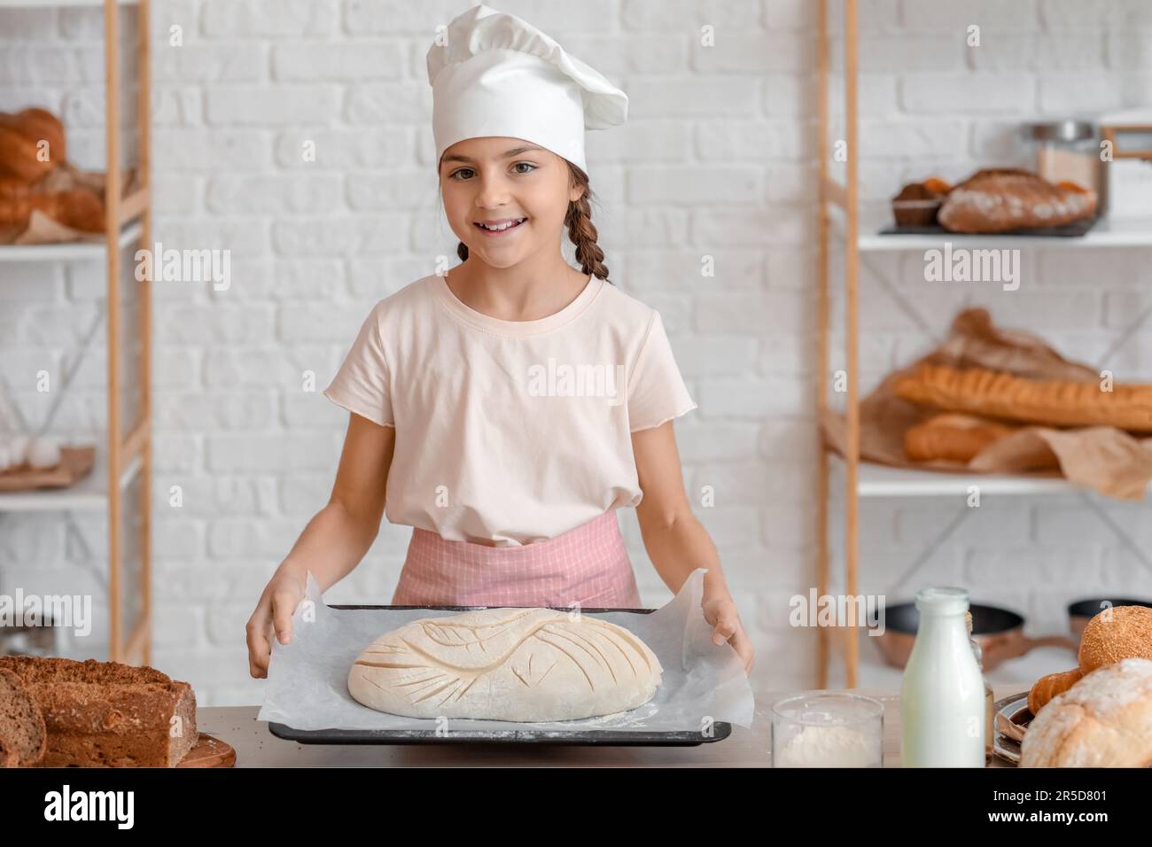 Little baker holding tray with raw bread in kitchen Stock Photo - Alamy