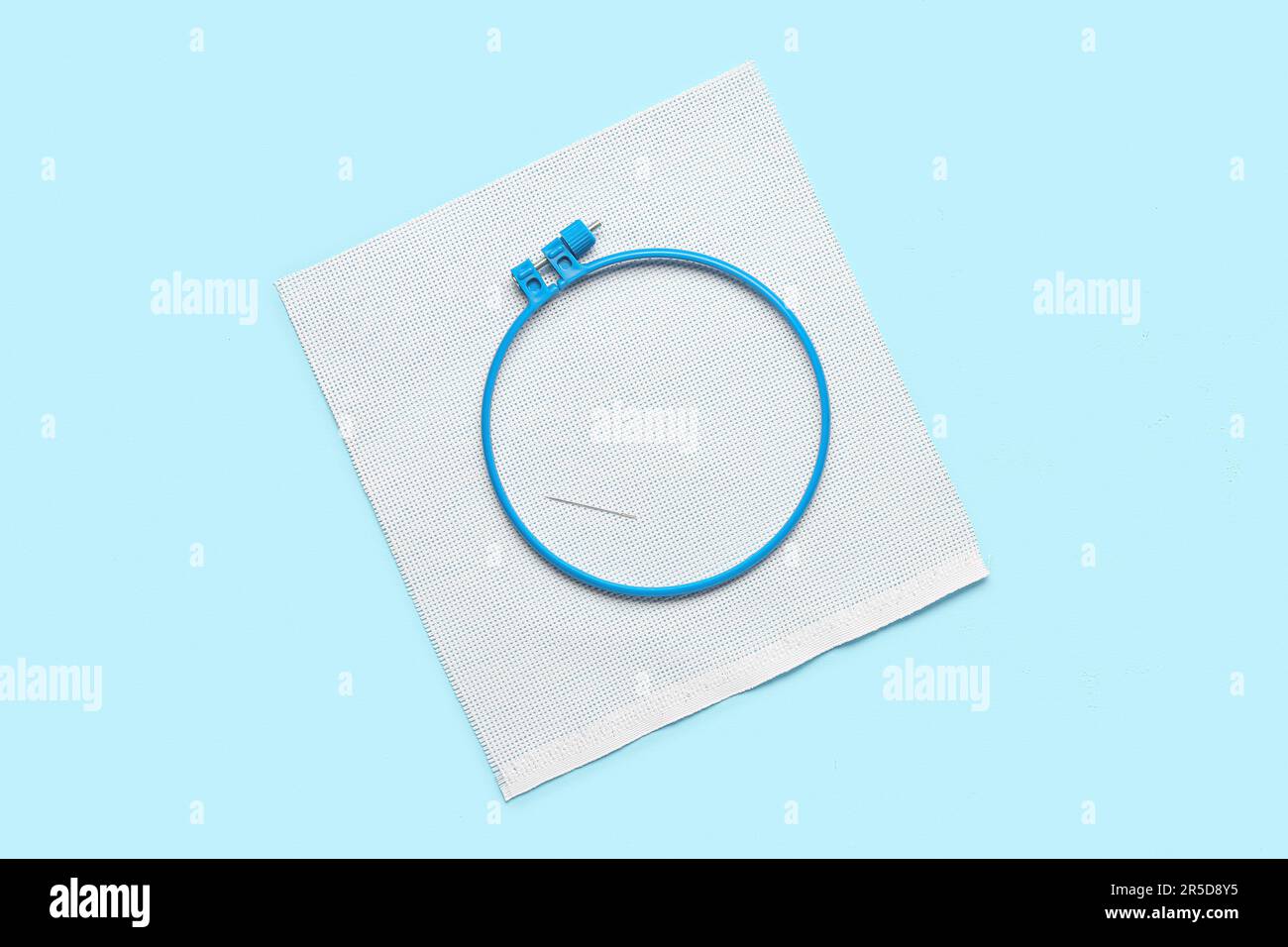 Plastic embroidery hoop with canvas and needle on blue background Stock ...