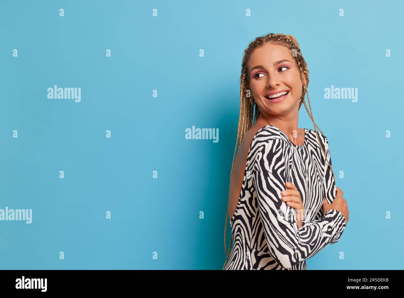 Young cute girl with long dreadlocks stands half-turned to the camera ...
