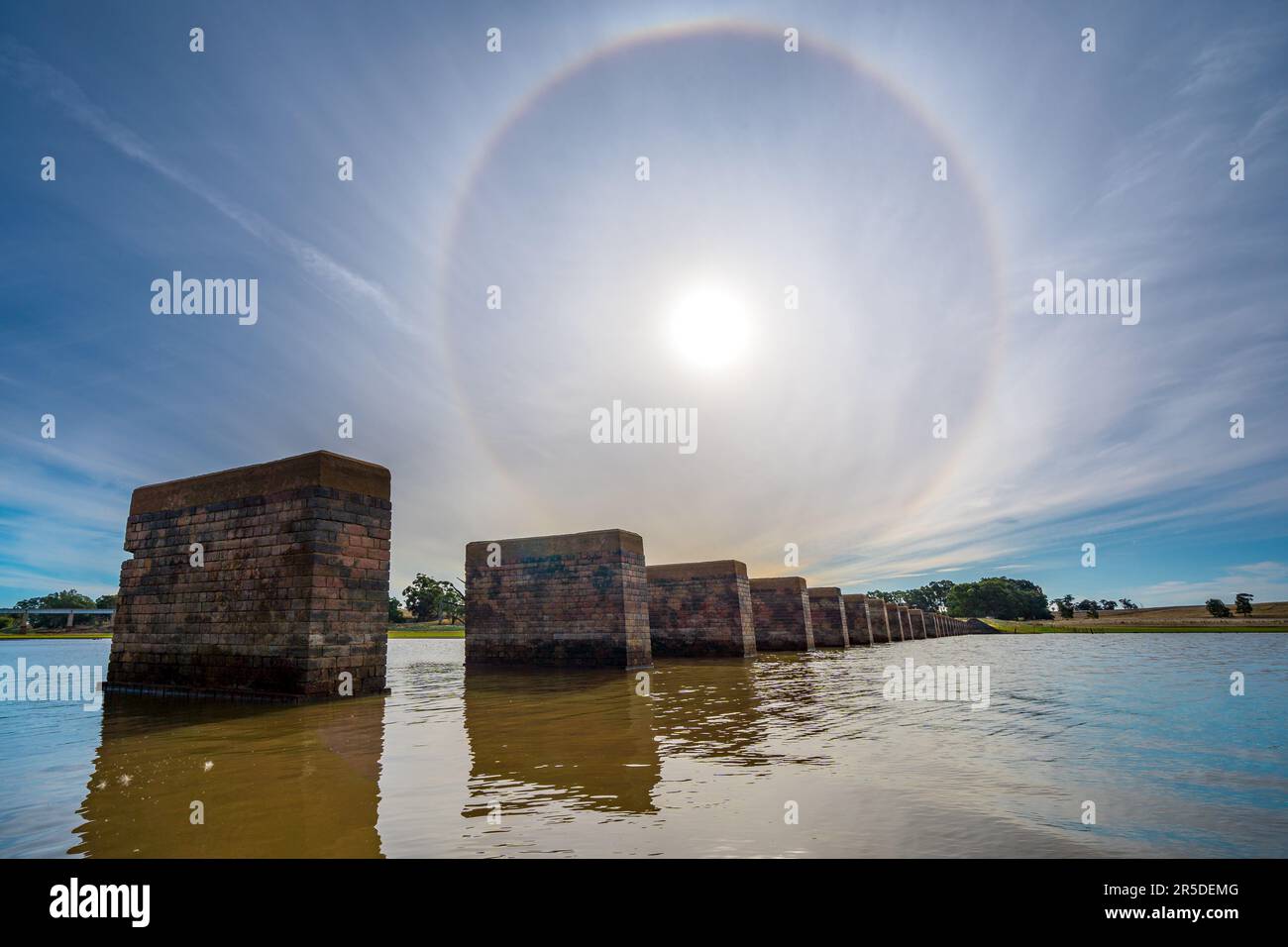 Low angled view of a Solar Halo over ruins of viaduct pillars in a lake ...