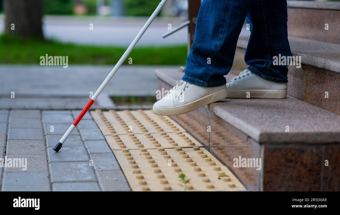 Close-up of female foot, walking stick and tactile tiles. Blind woman ...