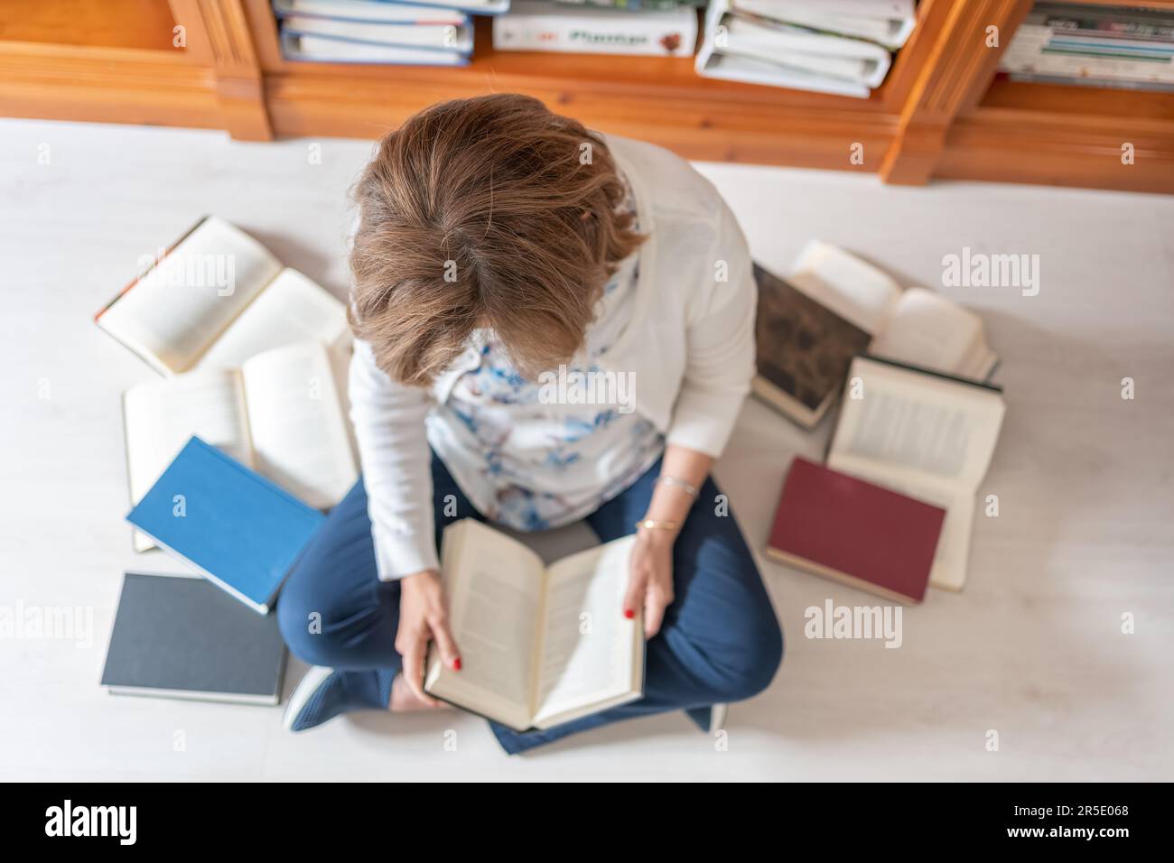 White woman sitting on the floor with a lot of books in an overhead ...
