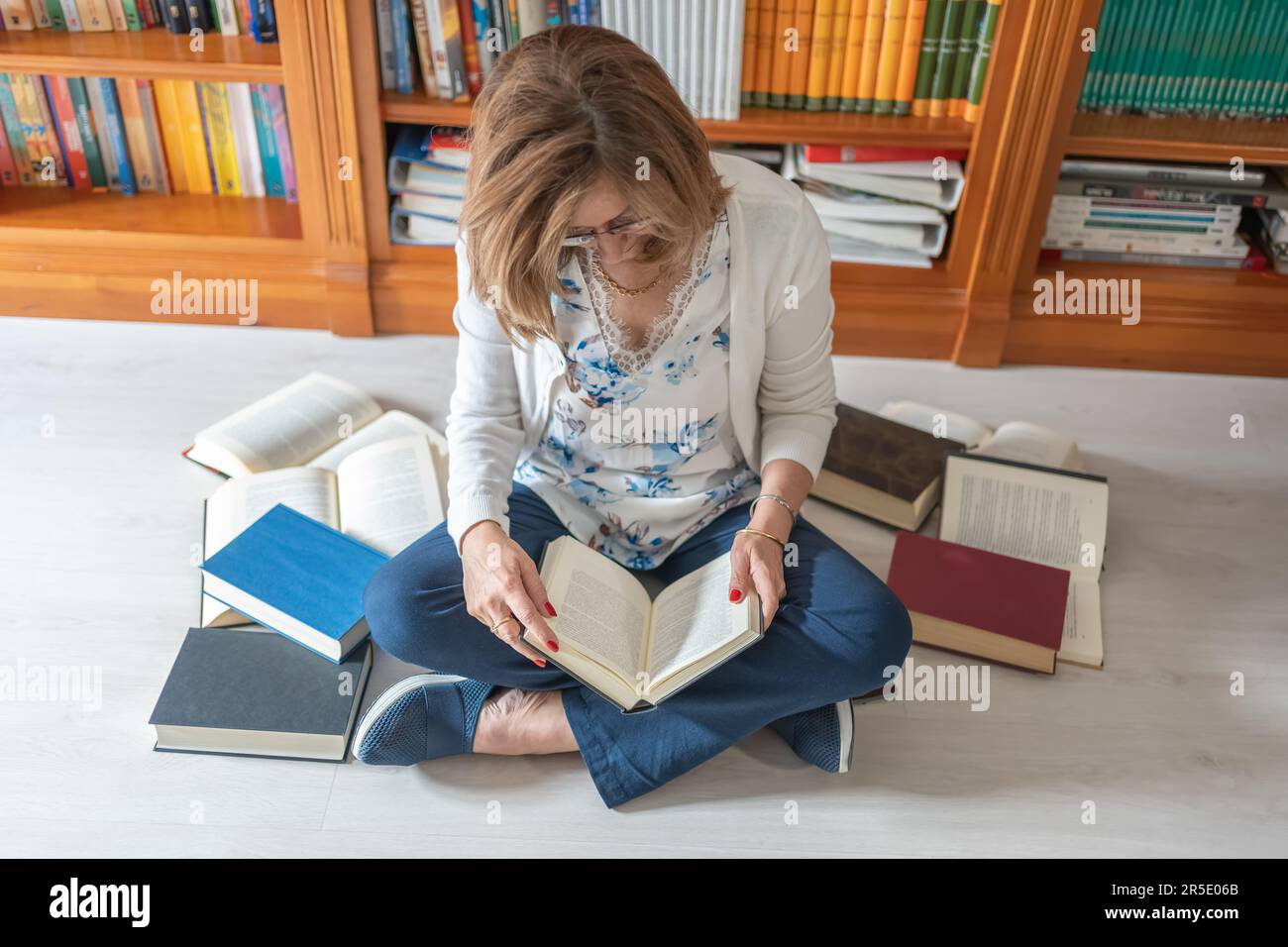 Senior woman sitting on the floor with lots of books around, reading ...