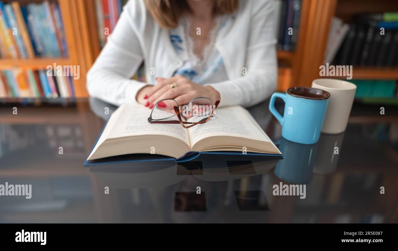 Open book on a glass table with glasses on the book and coffee cups ...