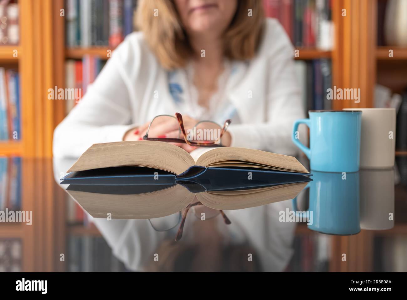 Open book on a glass table with glasses on the book and coffee cups ...