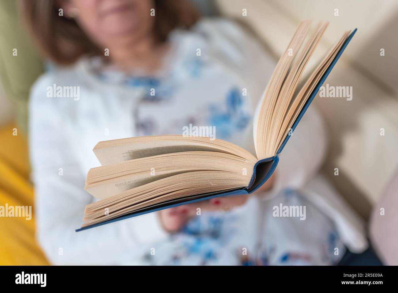 Woman lying on the sofa and detail of the book she is reading in a ...