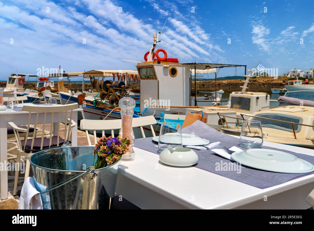 Tables and chairs of restaurant by waterfront with fishing boats in ...