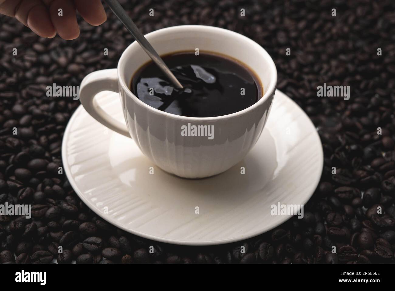 Hand holding coffee stirring spoon in white cup on table. Black coffee ...