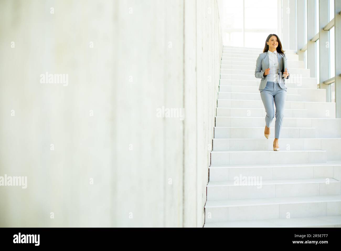 Young business woman walking down the stairs and holding laptop at the ...