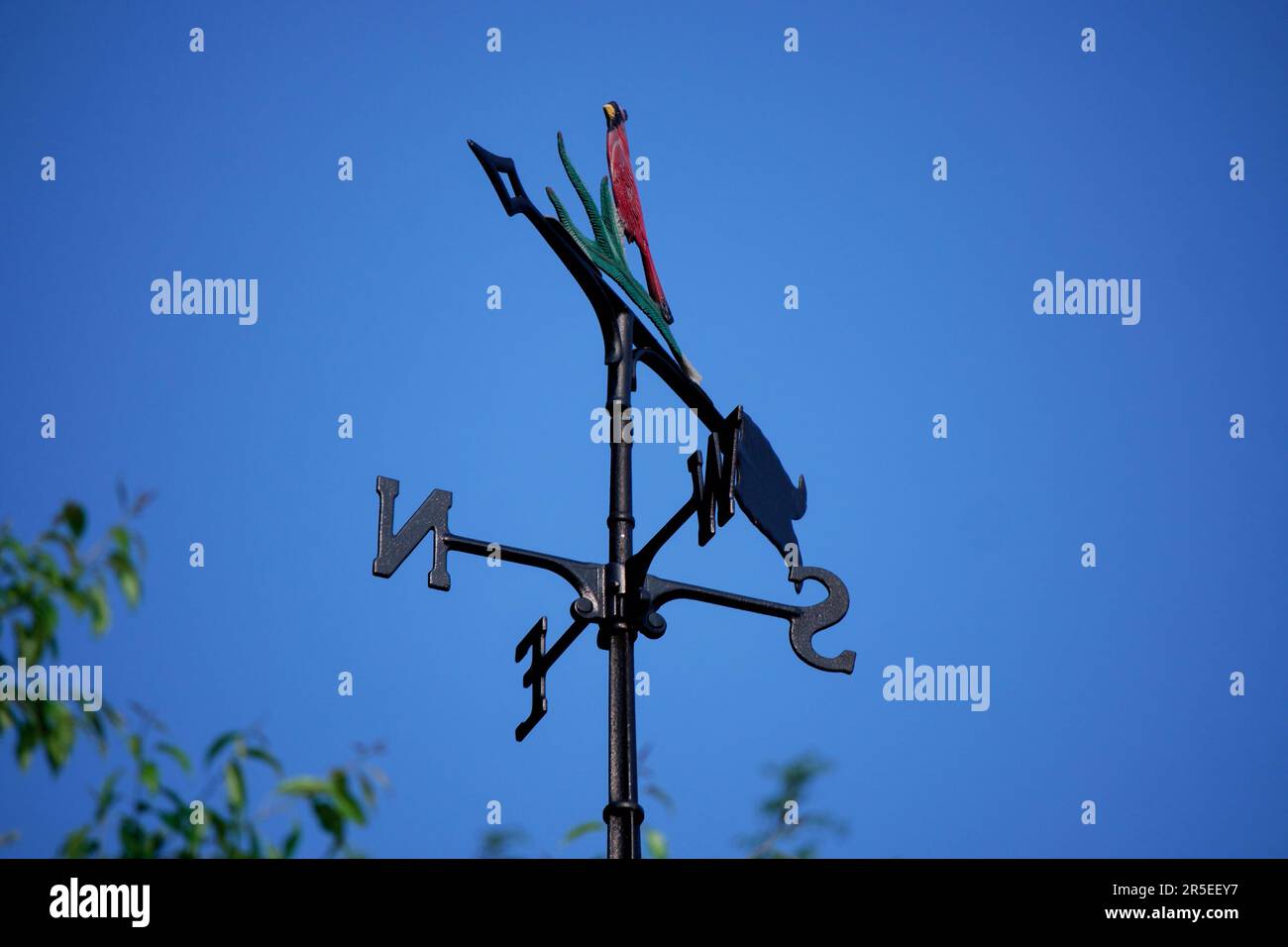 A traditional metal weather vane silhouetted against a bright blue sky ...