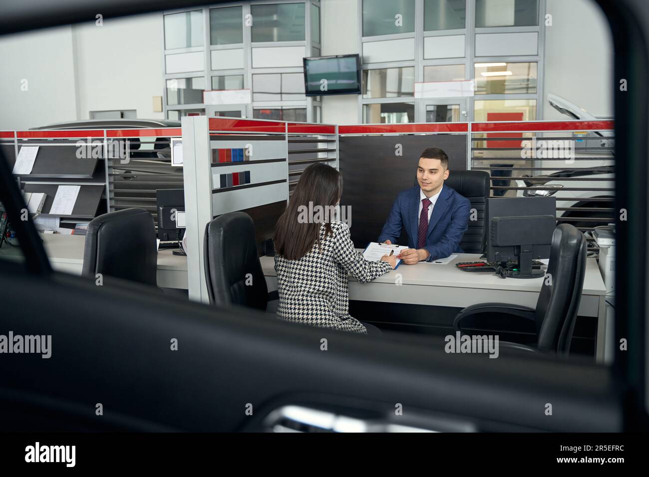 Young brunette woman and car dealership manager communicate in office ...