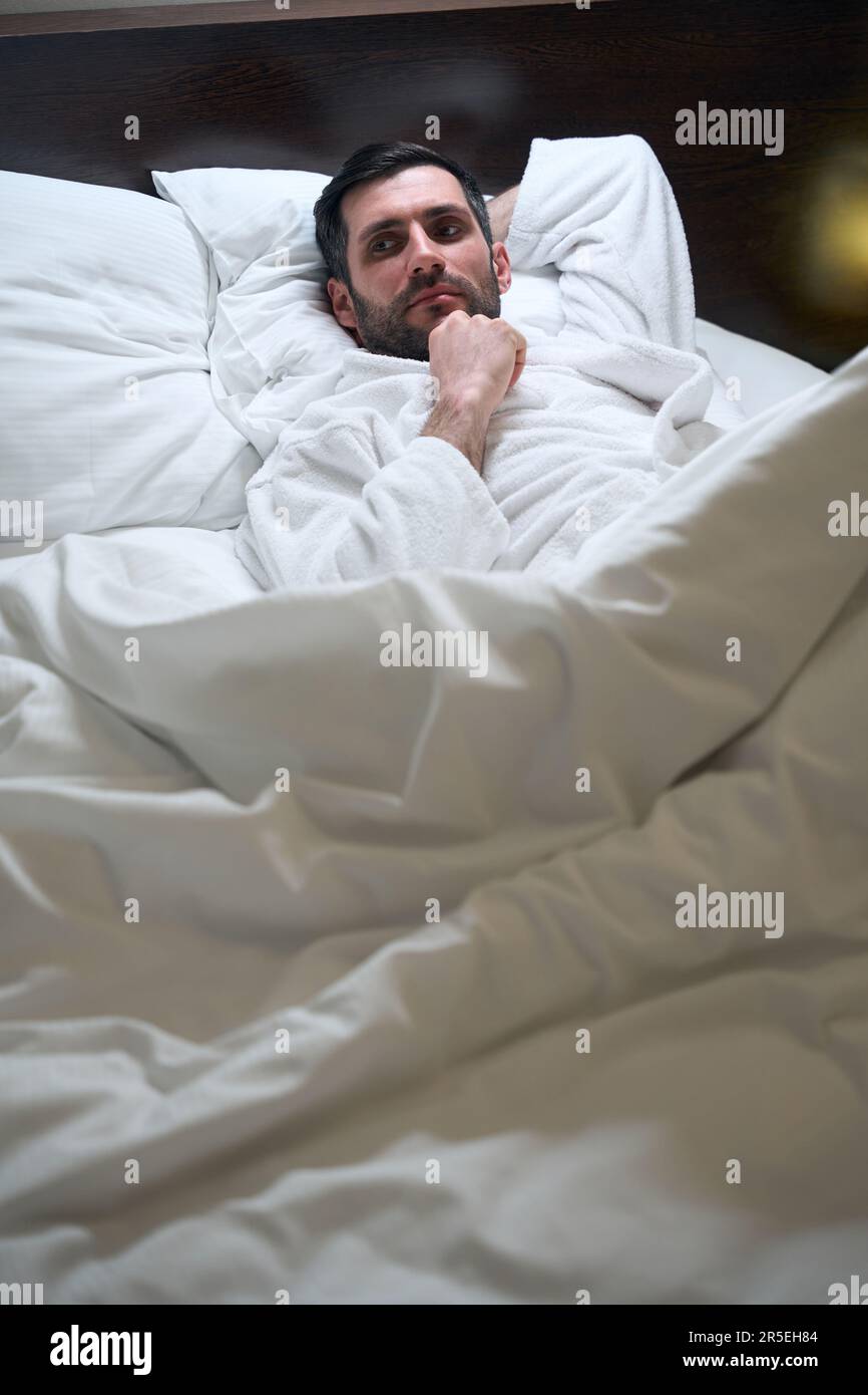 Sad man lies in bed on soft pillows in hotel room Stock Photo - Alamy