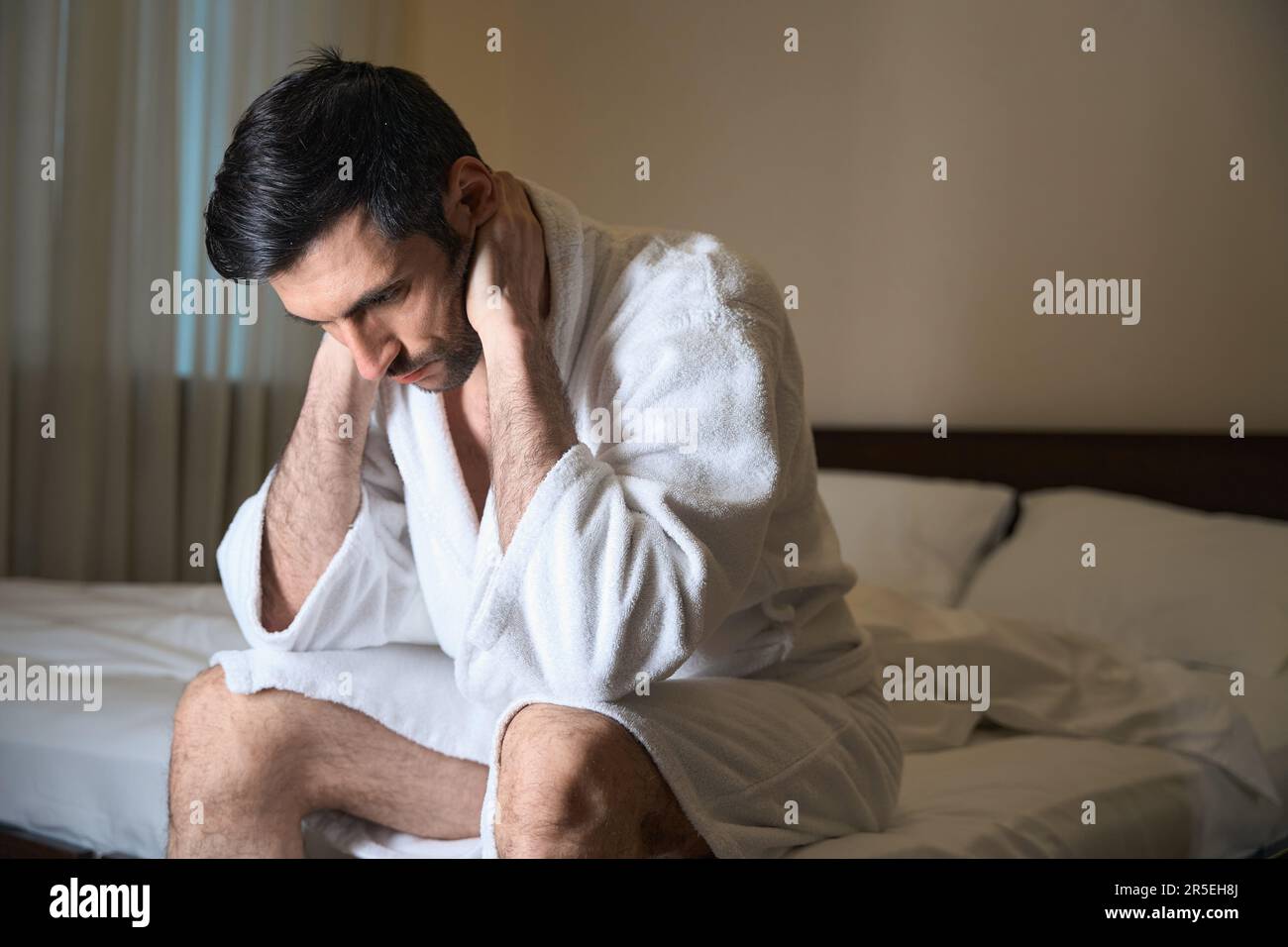 Suffering male sits on a large bed in hotel room Stock Photo - Alamy