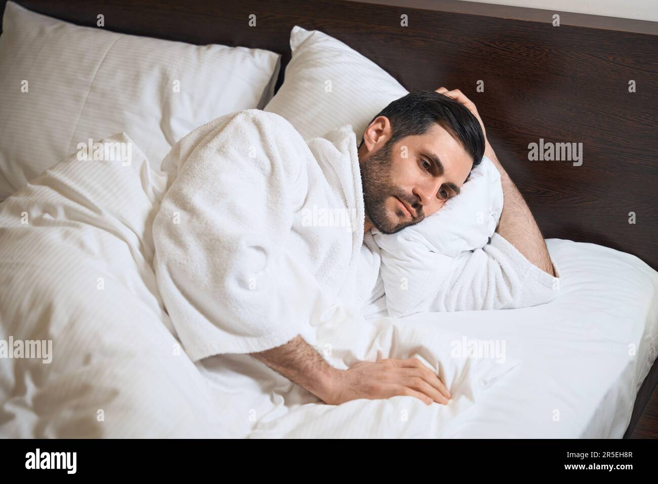 Tired hotel guest lies in bed on soft pillows Stock Photo - Alamy