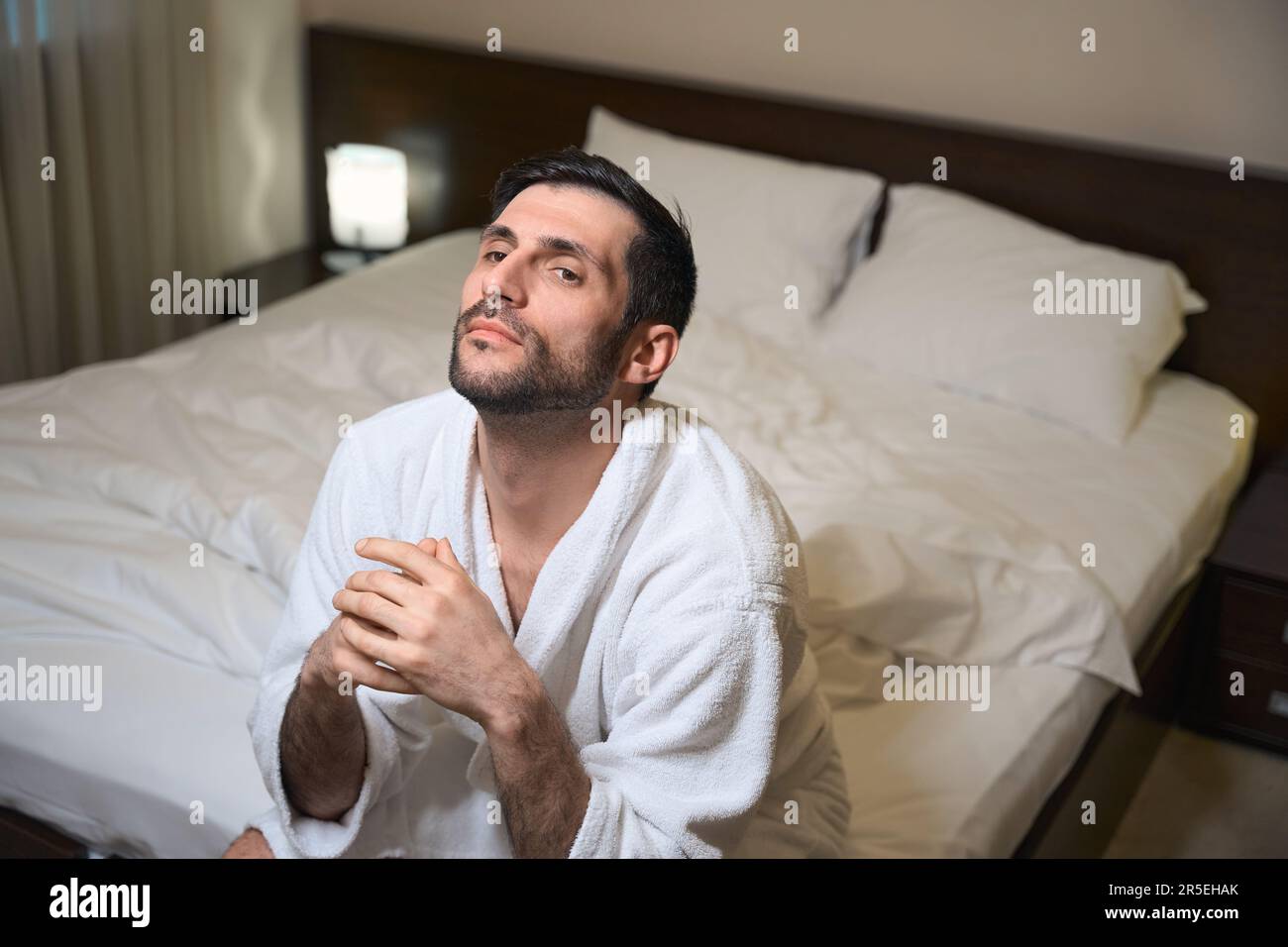 Sad man is sitting on a bed in hotel room Stock Photo - Alamy