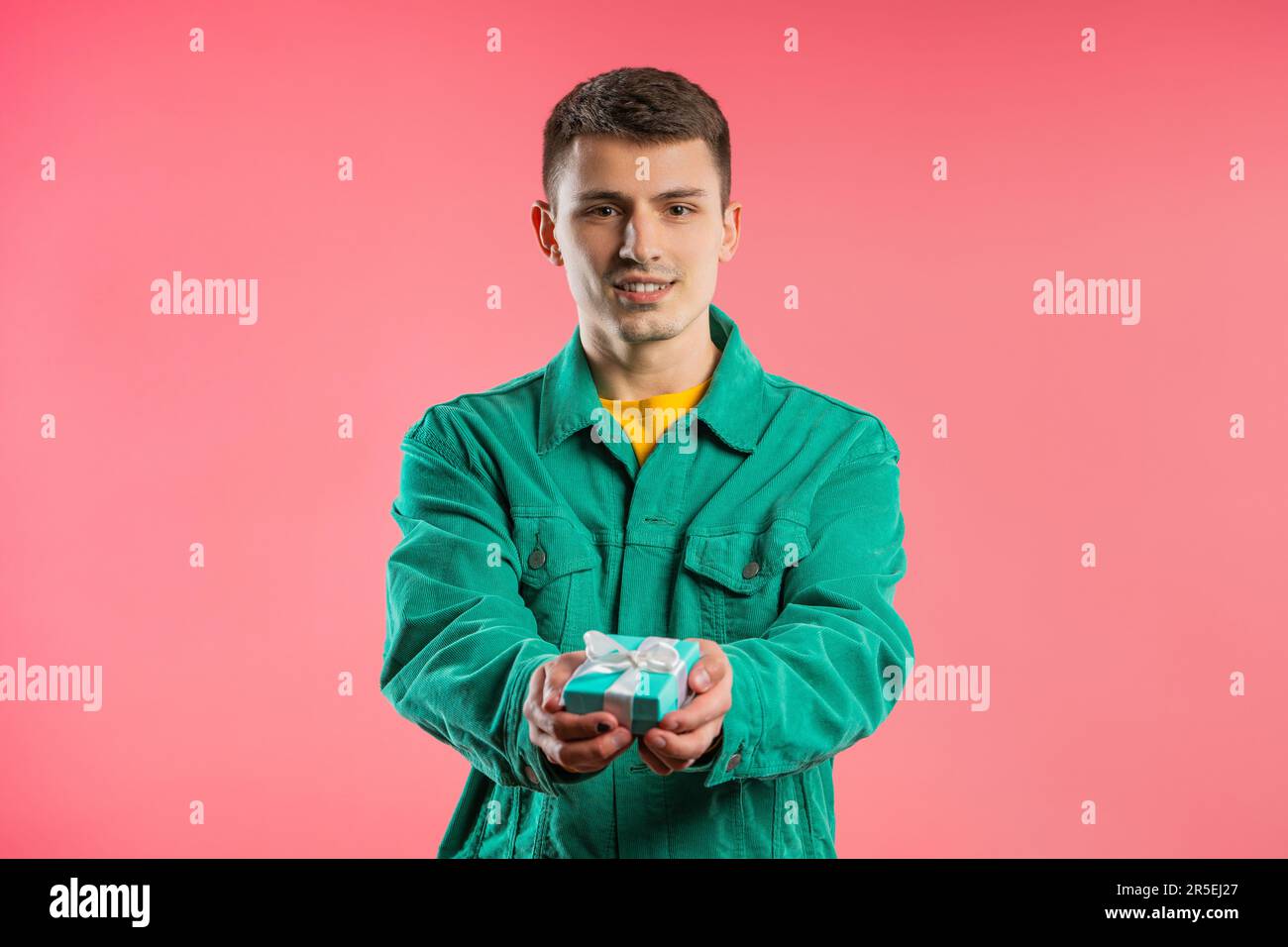 Man gives gift box by hands to camera, pink background. Guy smiling ...