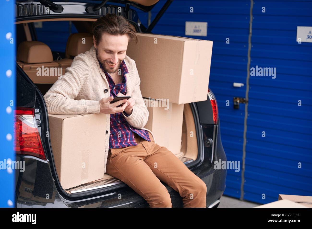 Smiling young guy with cardboard boxes in car trunk at storage ...