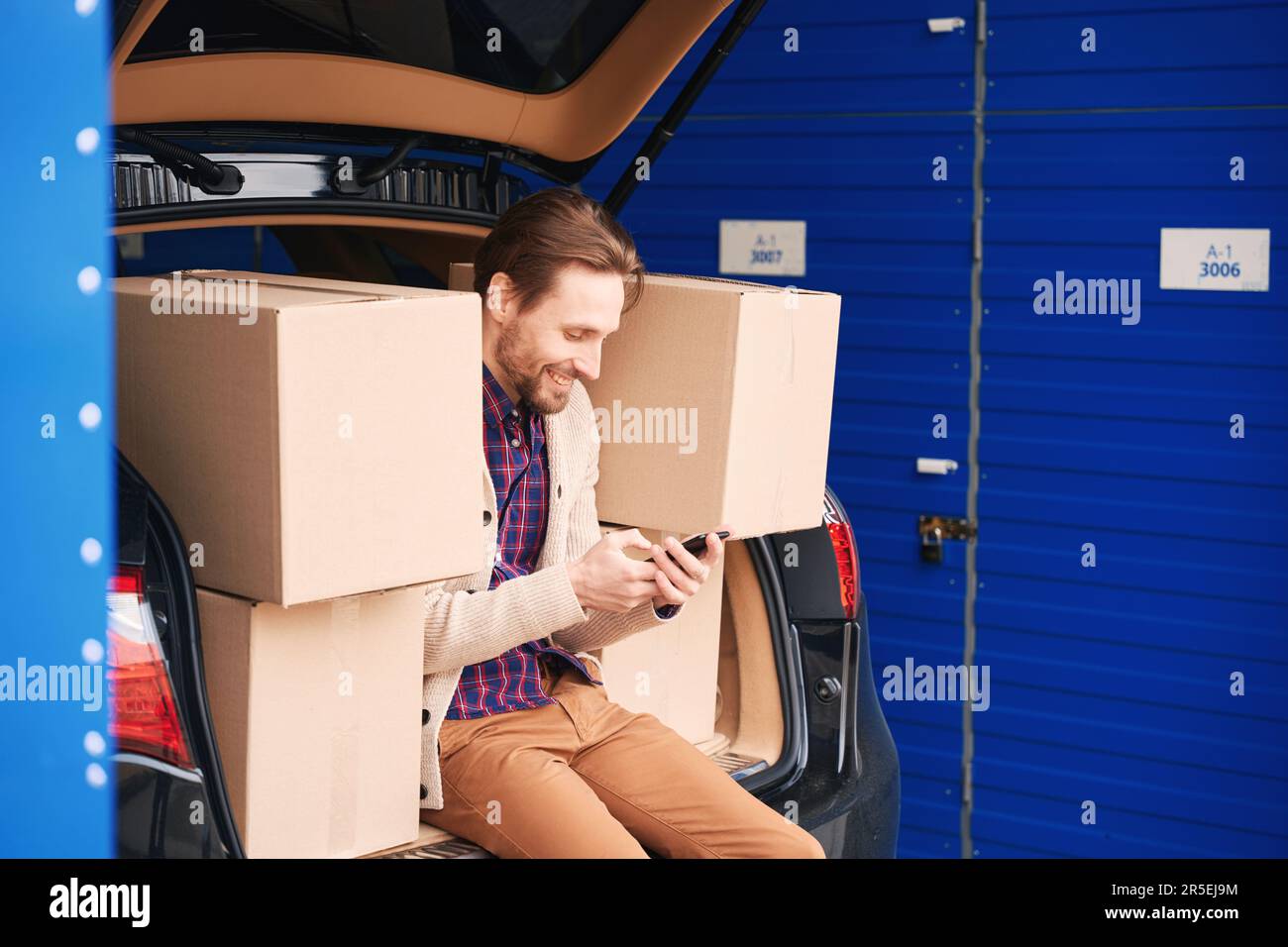 Young man with cardboard boxes in car trunk at storage warehouse Stock ...