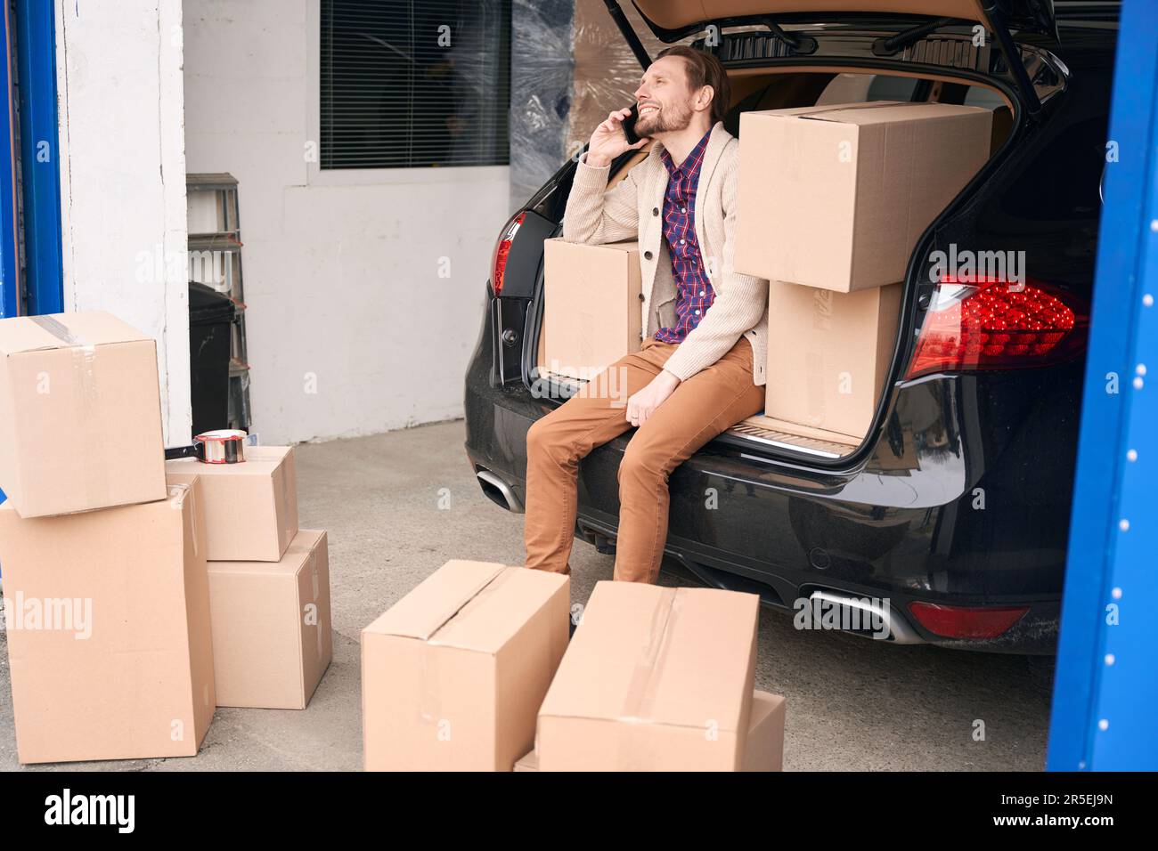 Side view of young guy with cardboard boxes in car trunk at storage ...