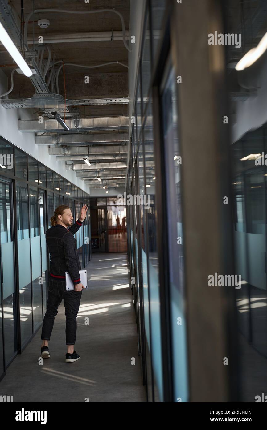 Attractive male employee waving hand in corridor Stock Photo - Alamy