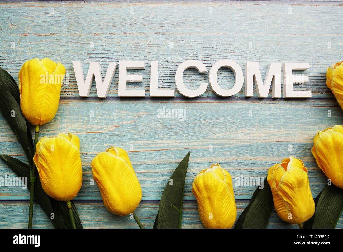 Welcome alphabet letters with yellow tulip flower on wooden background ...