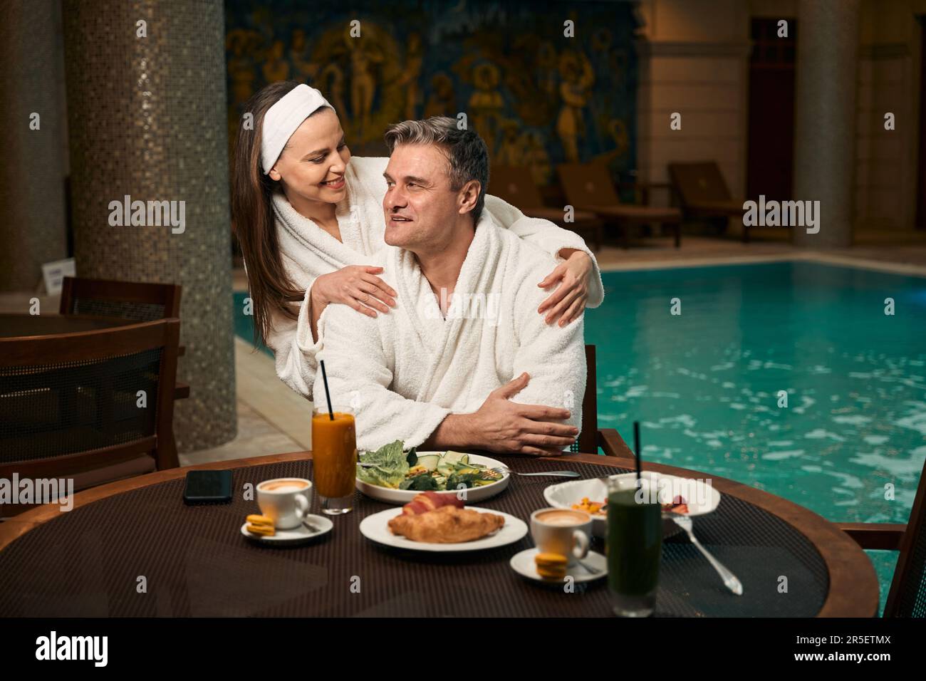 Happy lady embracing contented companion during lunch at spa resort ...