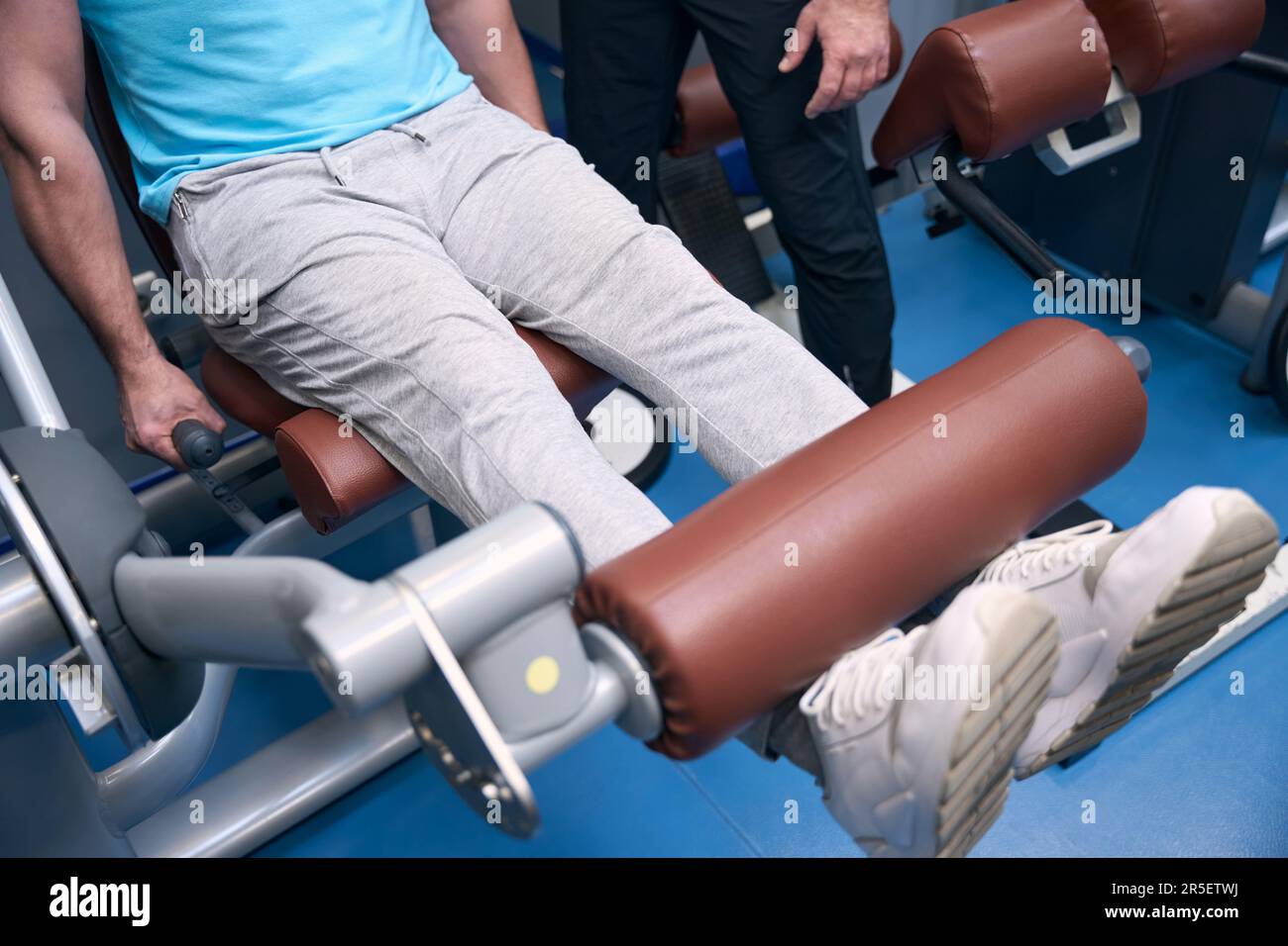 Sporty male doing lower body exercise supervised by fitness trainer ...