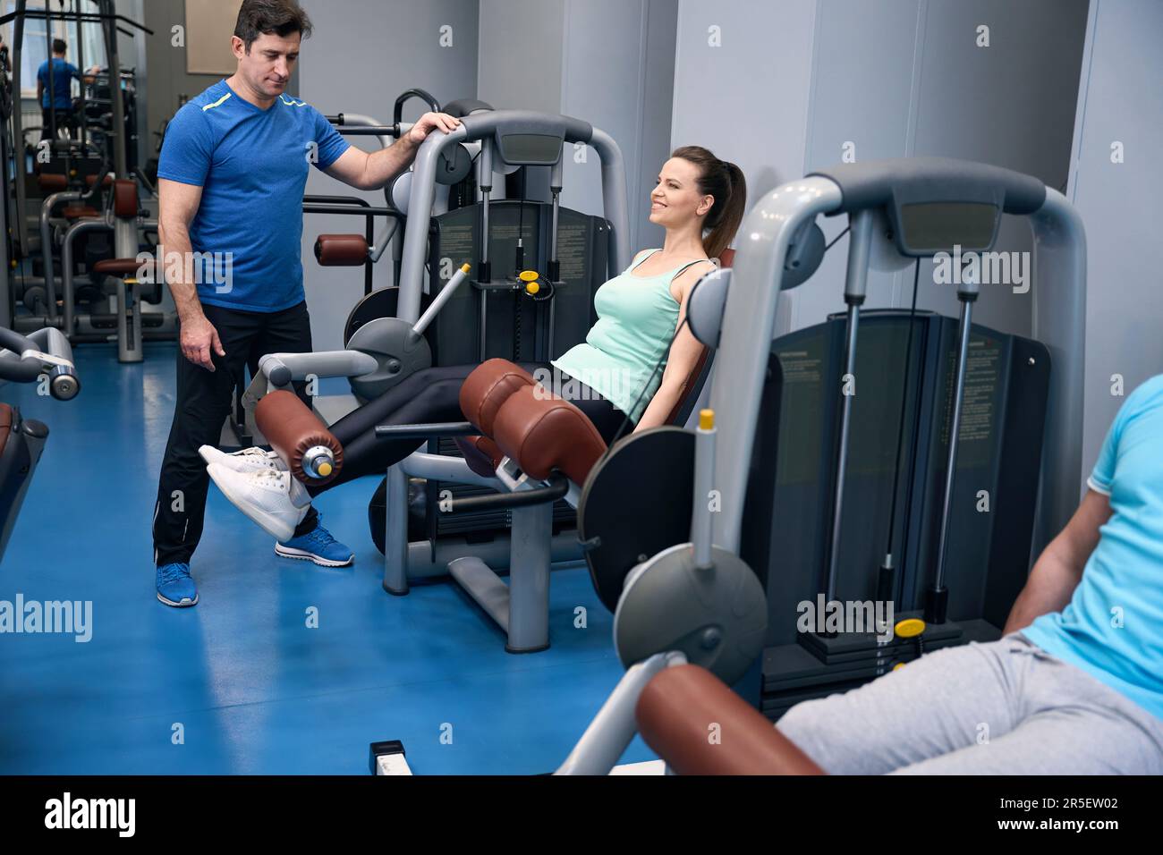 Smiling fit lady performing lower-body exercise supervised by coach ...