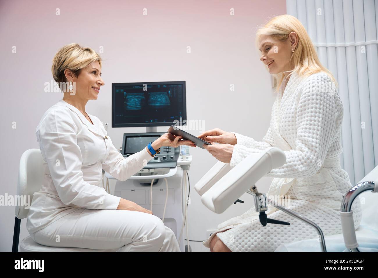 Gynecologist and patient use tablet against background of ultrasound ...