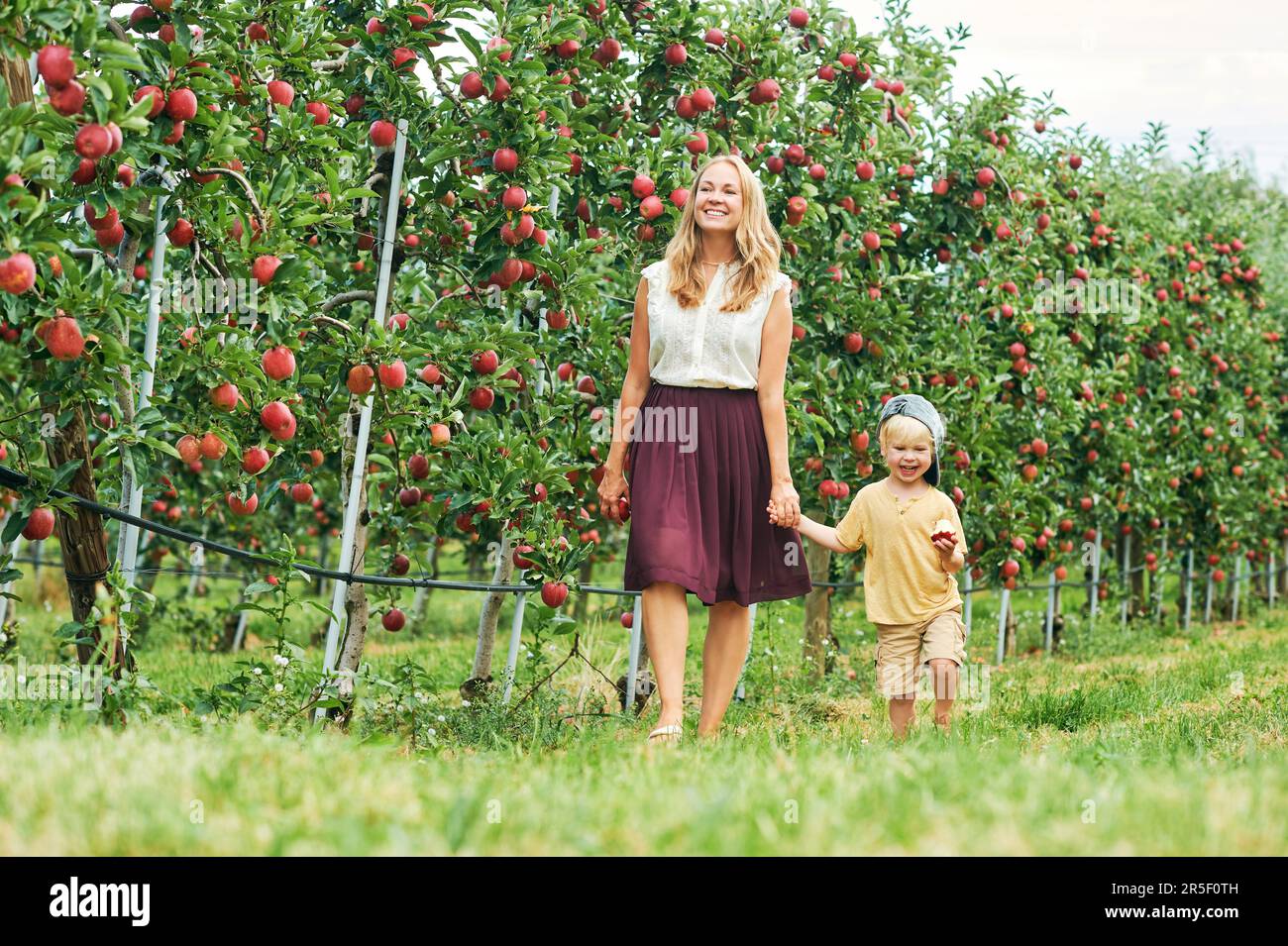 Outdoor portrait of happy young mother with little son walking in fruit ...
