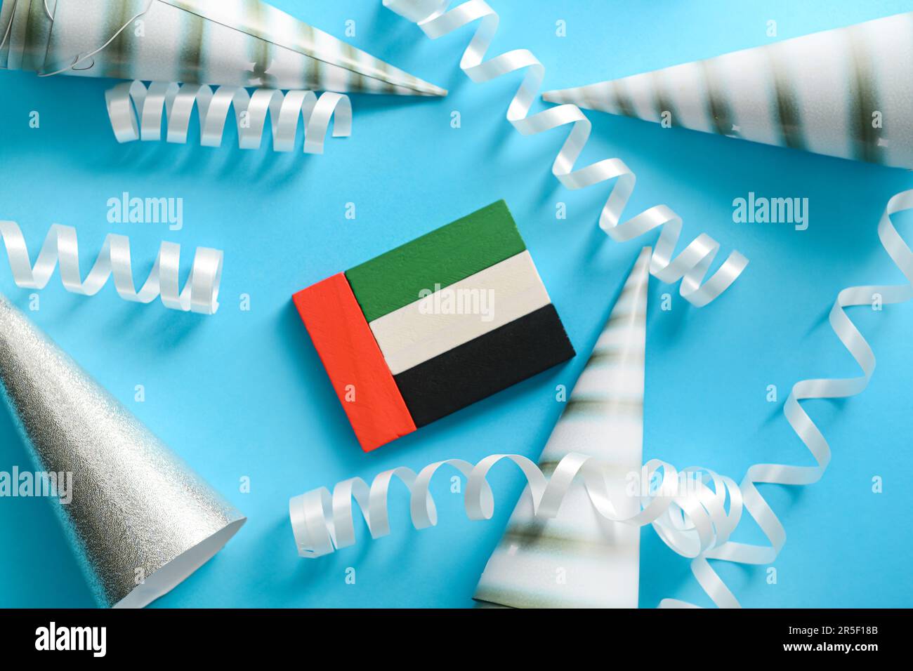 UAE flag made of blocks, ribbons and party hats on blue background ...