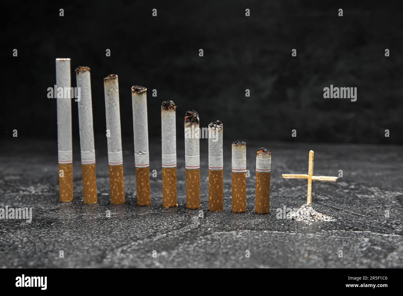 Row of cigarette butts and cross made of matches on dark background ...