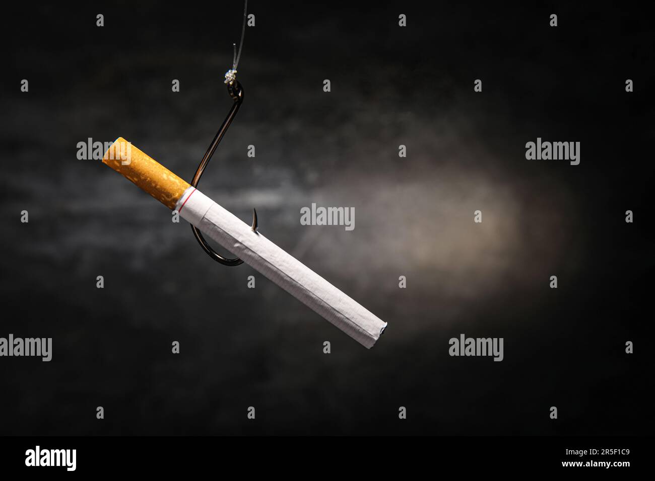 Cigarette hanging on hook against dark background. Stop smoking concept ...