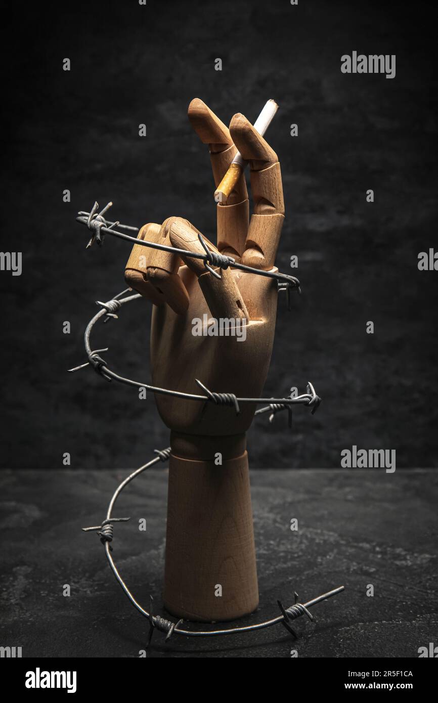 Wooden hand with cigarette and barbed wire on dark background. Stop ...