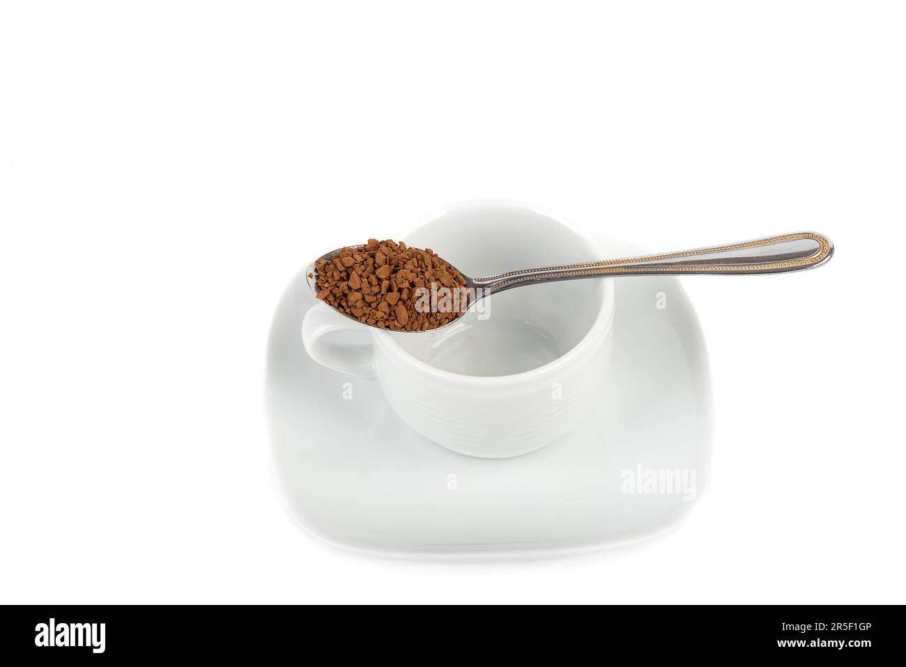Spoon full of granulated instant coffee over empty white cup and saucer ...