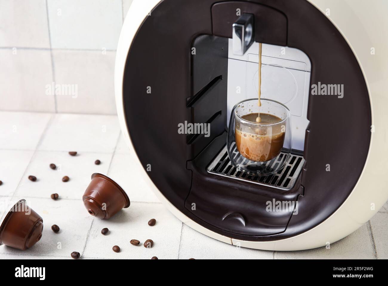 Modern capsule coffee maker with dripping espresso, cup, pods and beans ...