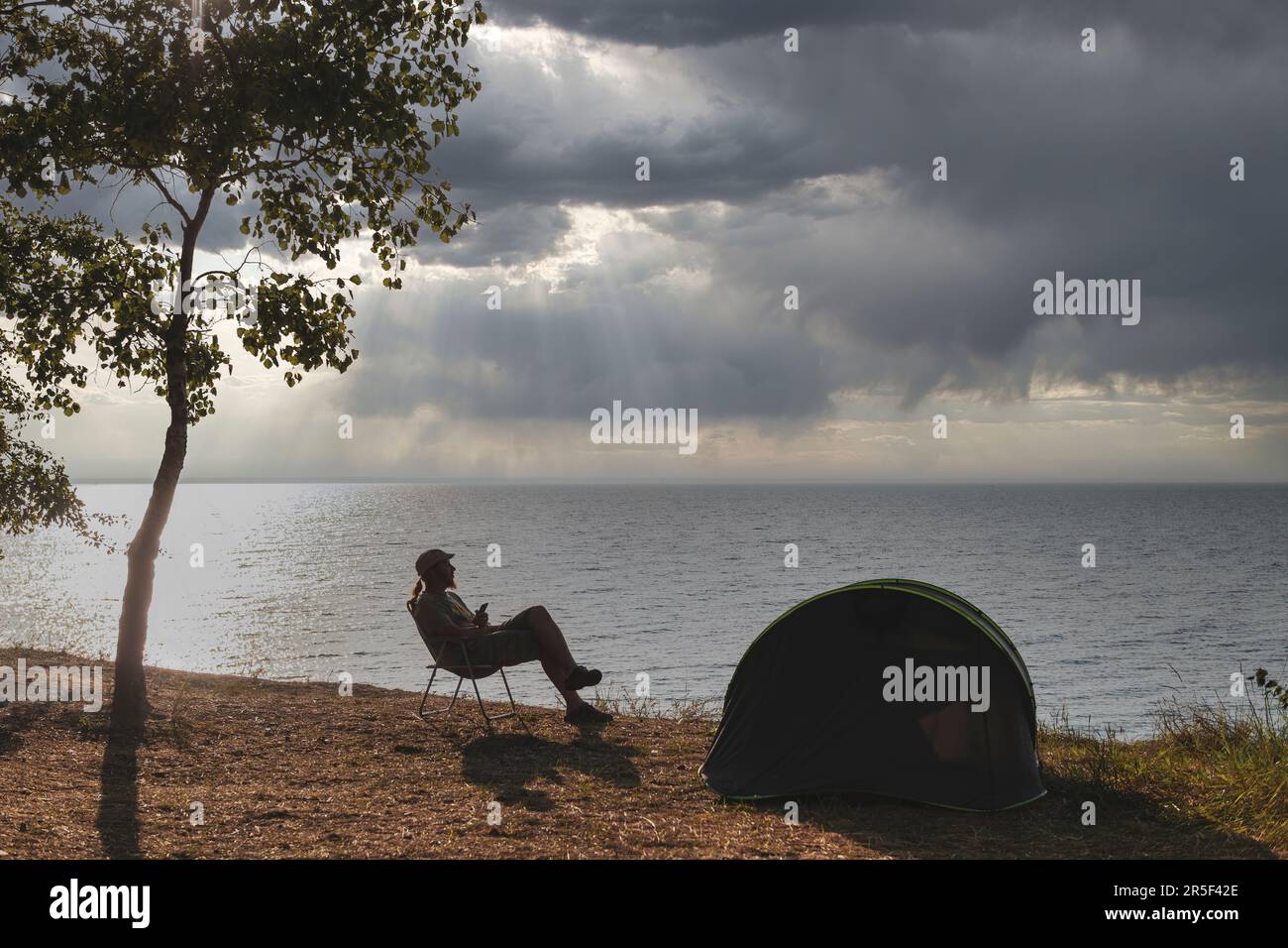 Lonely man sitting on the folding chair at the sea coast enjoys the ...