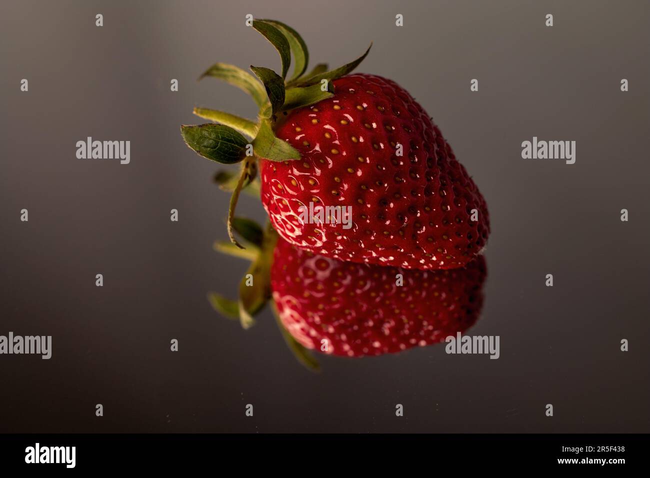 A red ripe strawberry on a mirror. Isolated close-up detail shot, dark ...