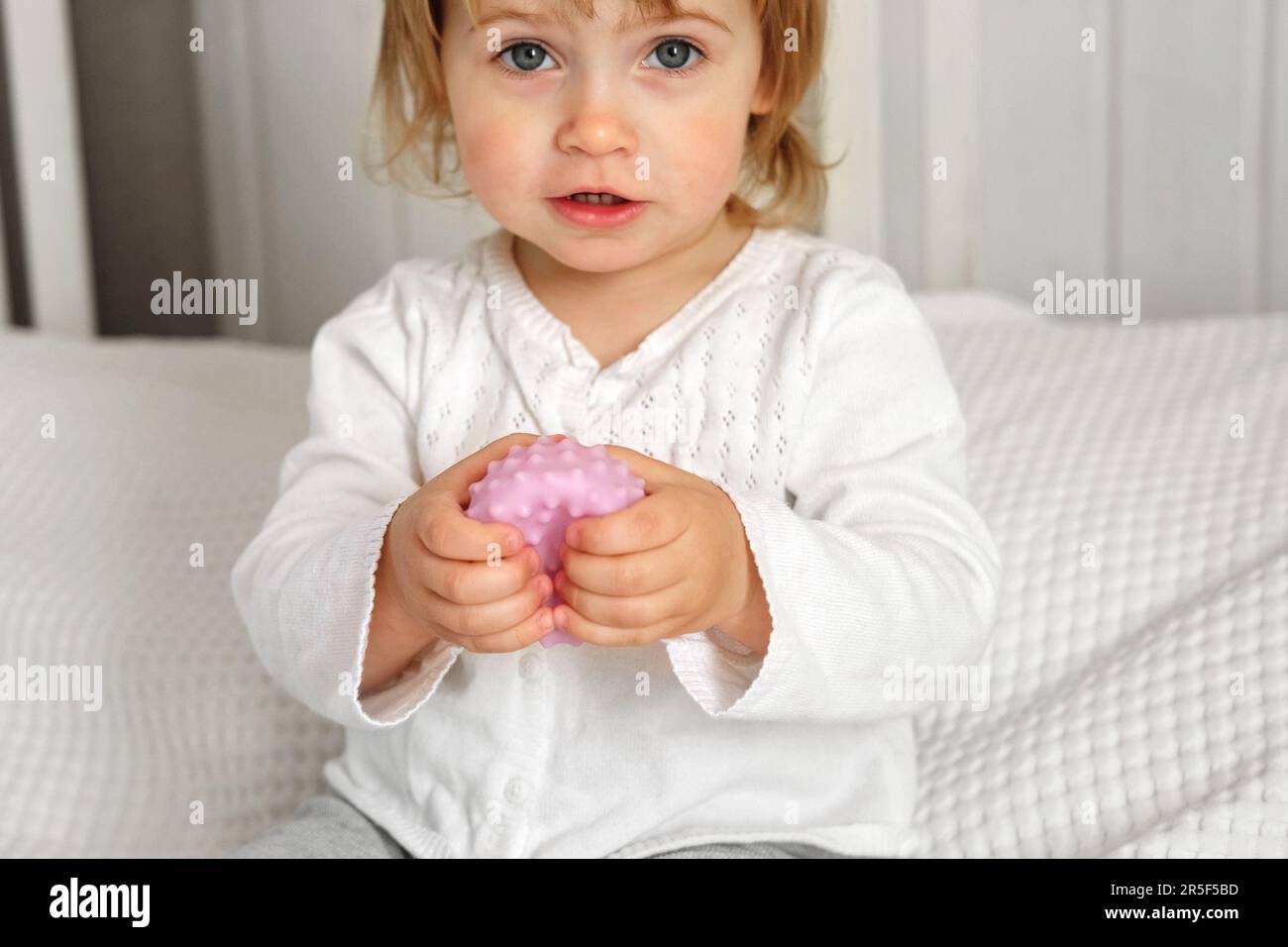 Cute baby girl playing tactile knobby balls. Young child hand plays ...