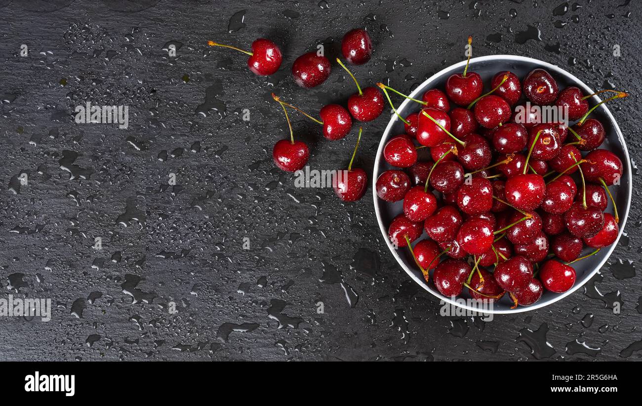 Fresh red ripe sweet cherry with water drops on plate on black slate ...