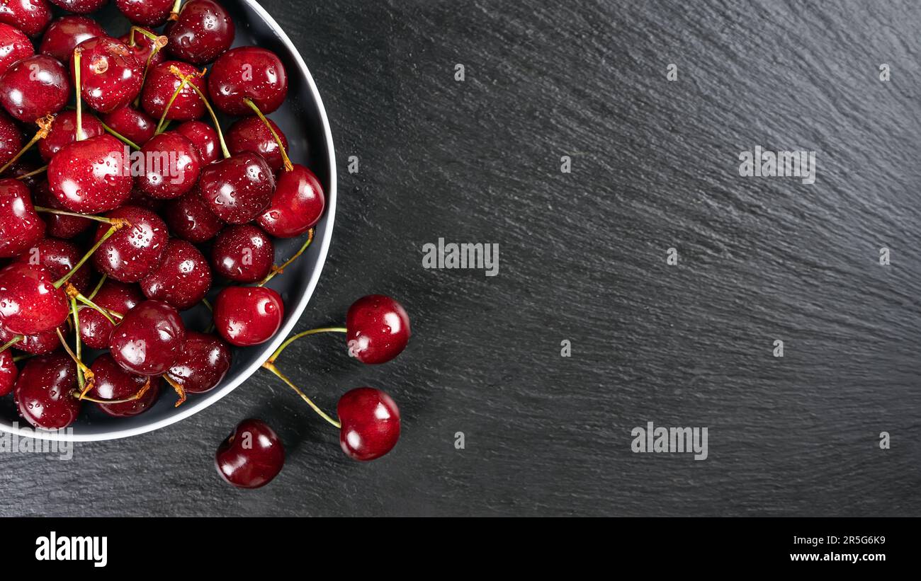 Fresh red ripe sweet cherry with water drops on plate on black slate ...