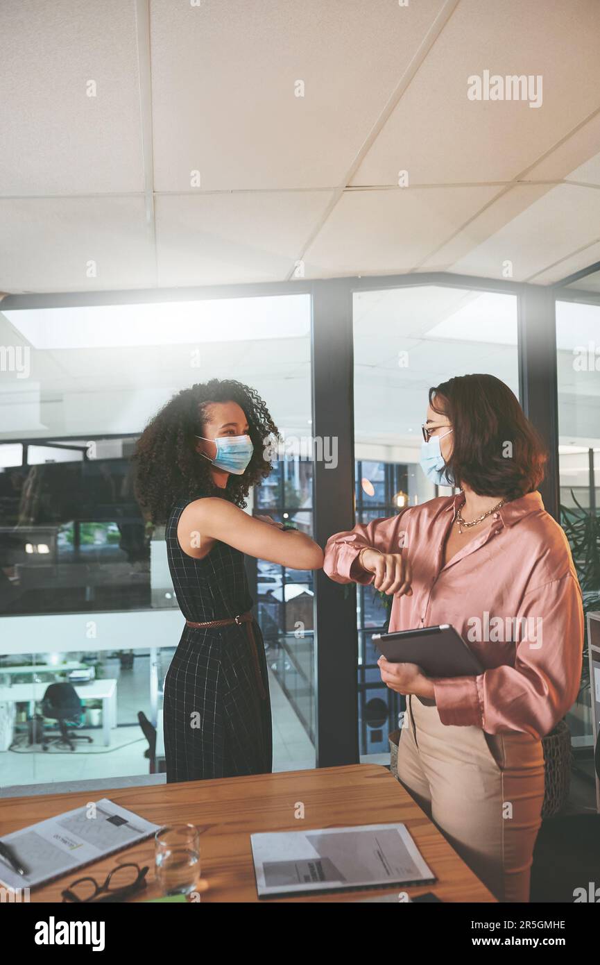 Elbow bumps are the new normal during Covid. two businesswomen standing ...