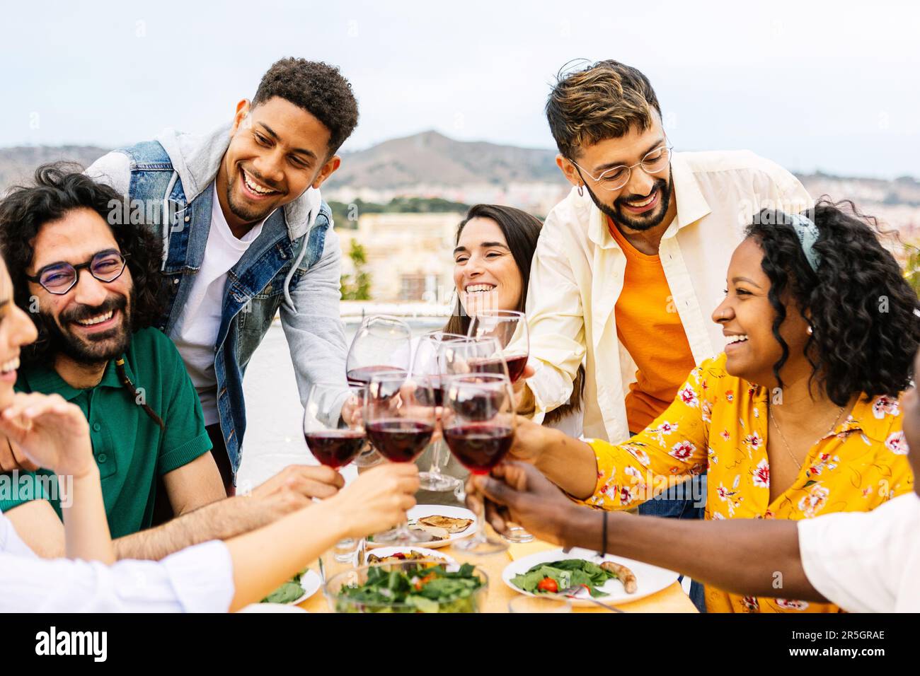 Group of young smiling people toast with red wine glasses at terrace ...