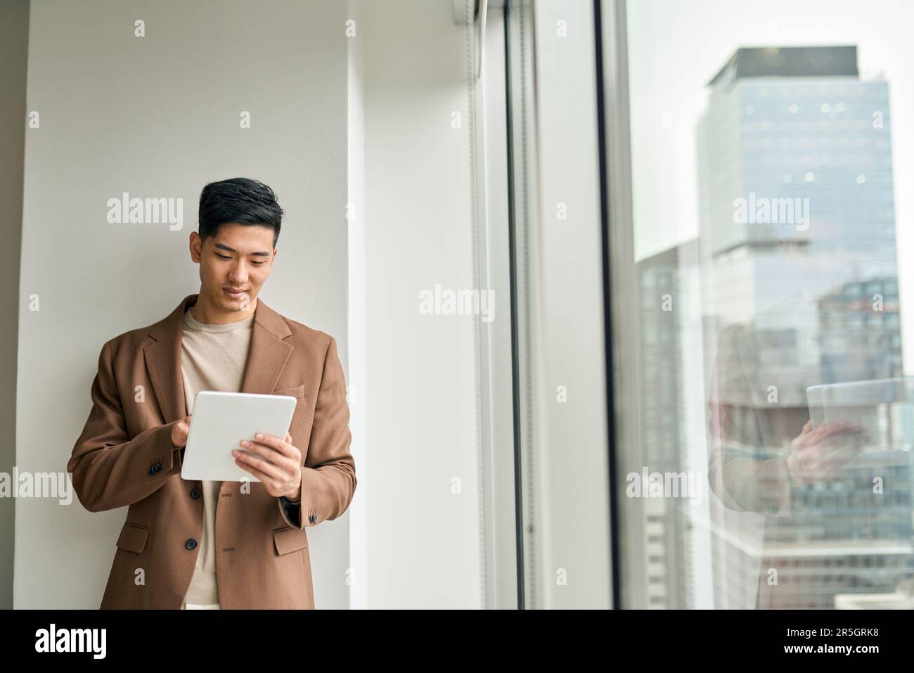 Young Japanese business man holding digital tablet standing near office ...