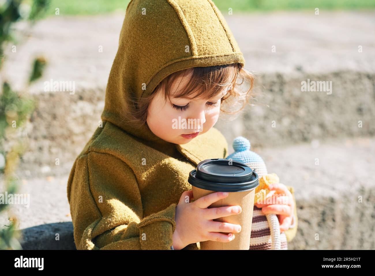 Funny little kid drinking from takeaway coffe cup in early morning ...